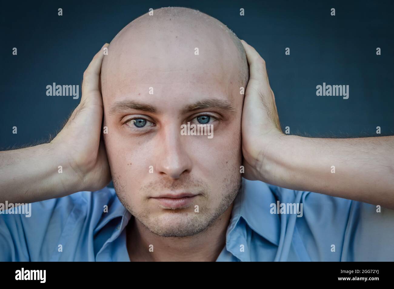 portrait of a young bald man with his hands covering his ears not to ...