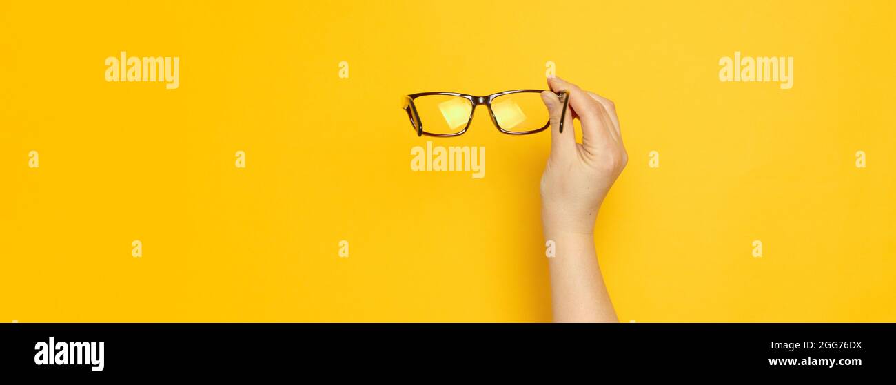 Hands hold stylish creative glasses for vision on yellow background ...