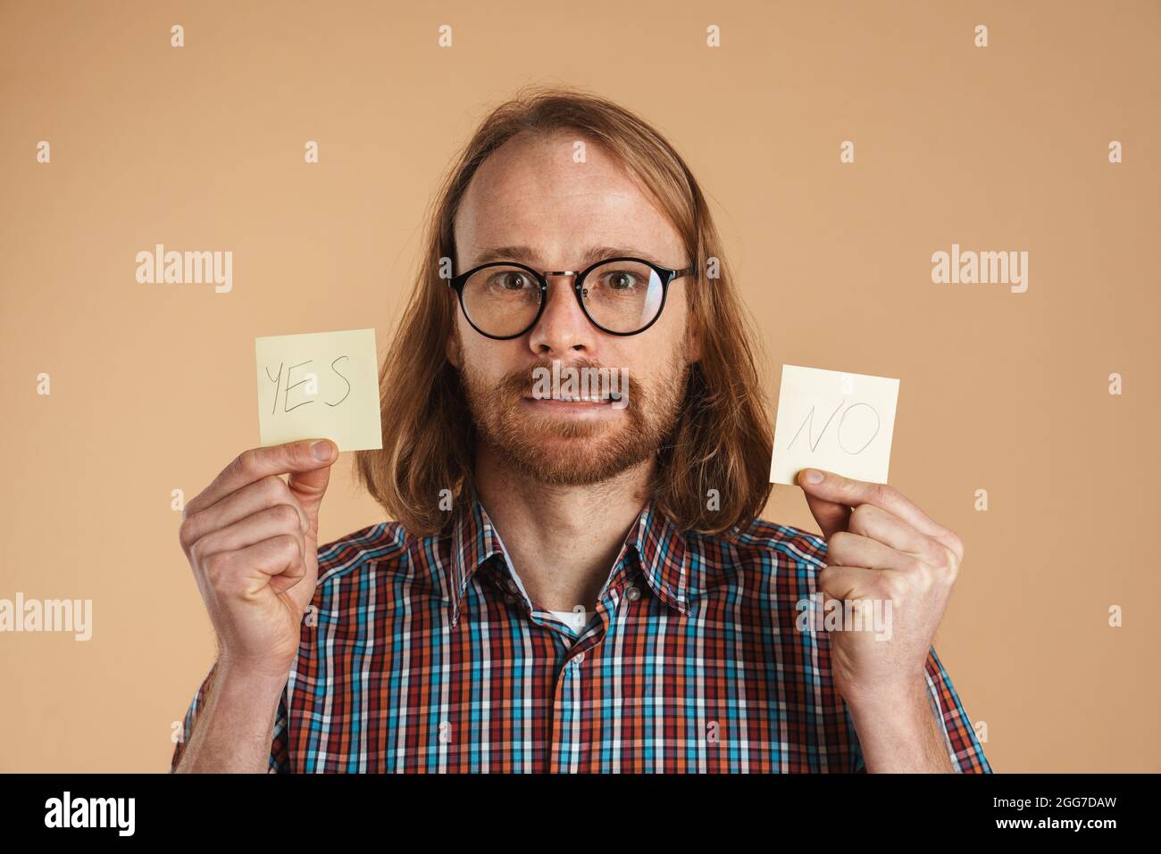 Confused ginger man showing piece of paper with yes and no signs ...