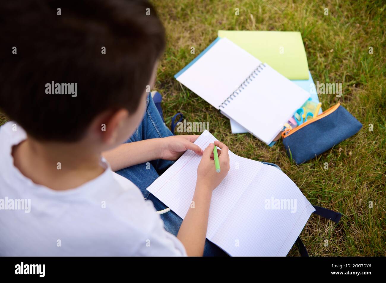 Overhead view of school boy writing on empty blank sheets of a workbook ...