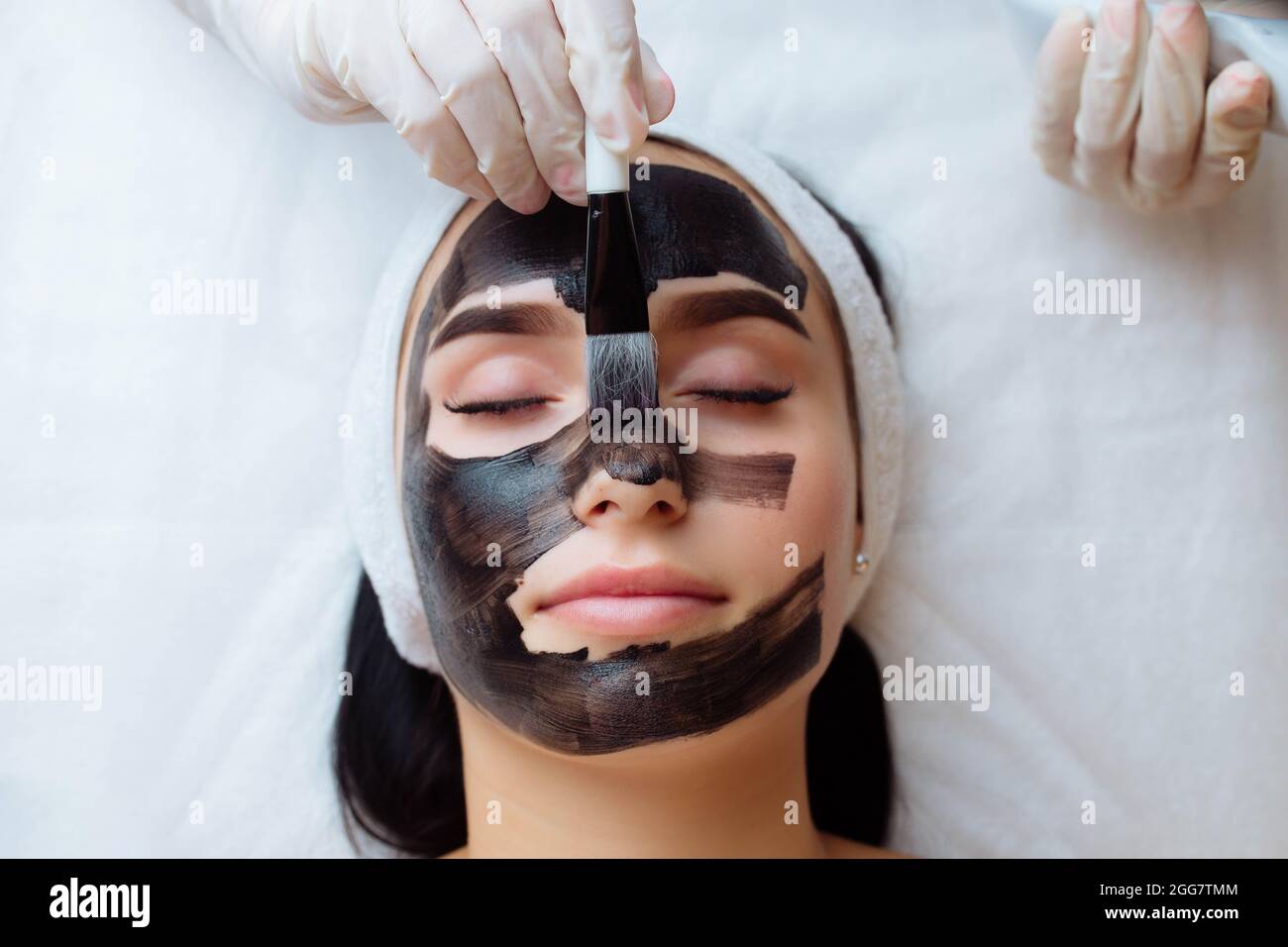 cosmetologist applying black mask on pretty woman face wearing black ...