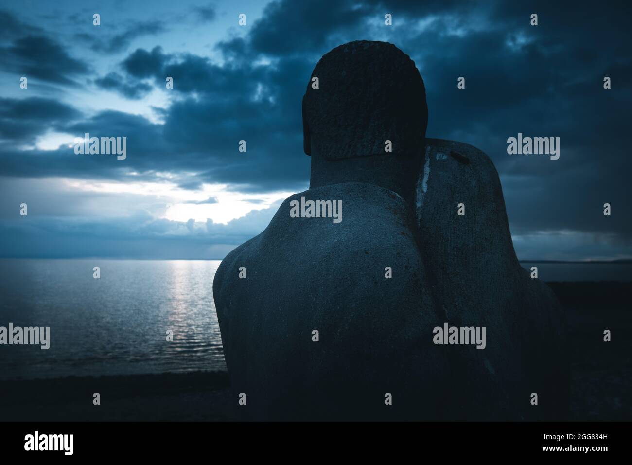 A closeup of a statue of a person on the shore of the sea in the ...