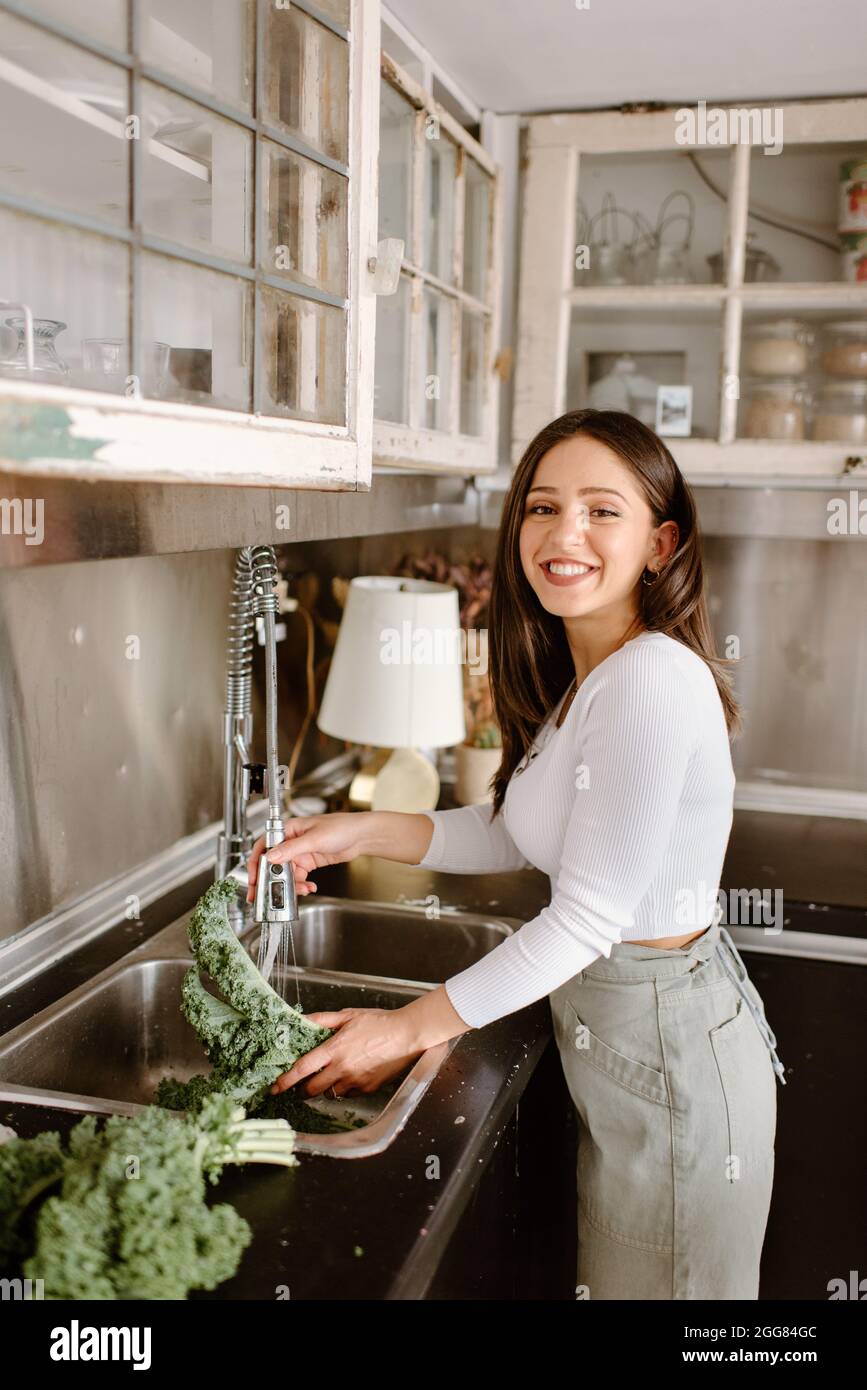 Smiling young woman washing kale in kitchen sink Stock Photo - Alamy