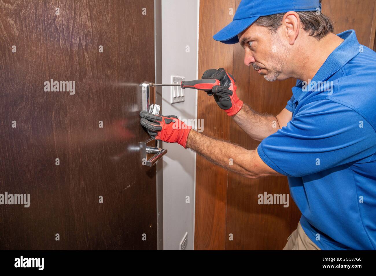 Locksmith using a screwdriver on a deadbolt lock, side view, wearing ...