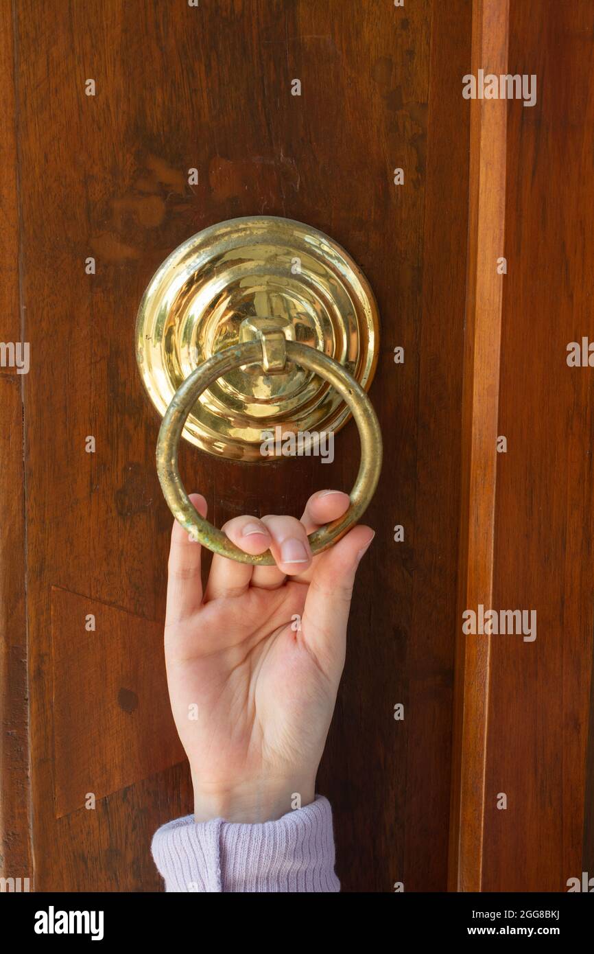 Female's hand knocking on a door with an old metal knocker on a wooden ...