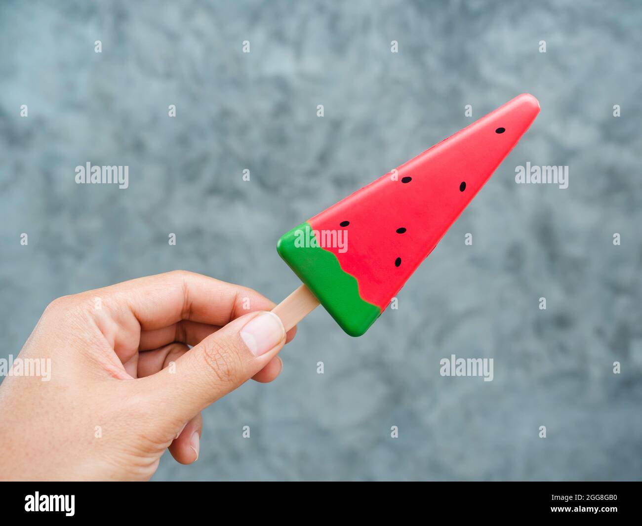 Close-up hand holding artificial watermelon slice popsicle on grey ...