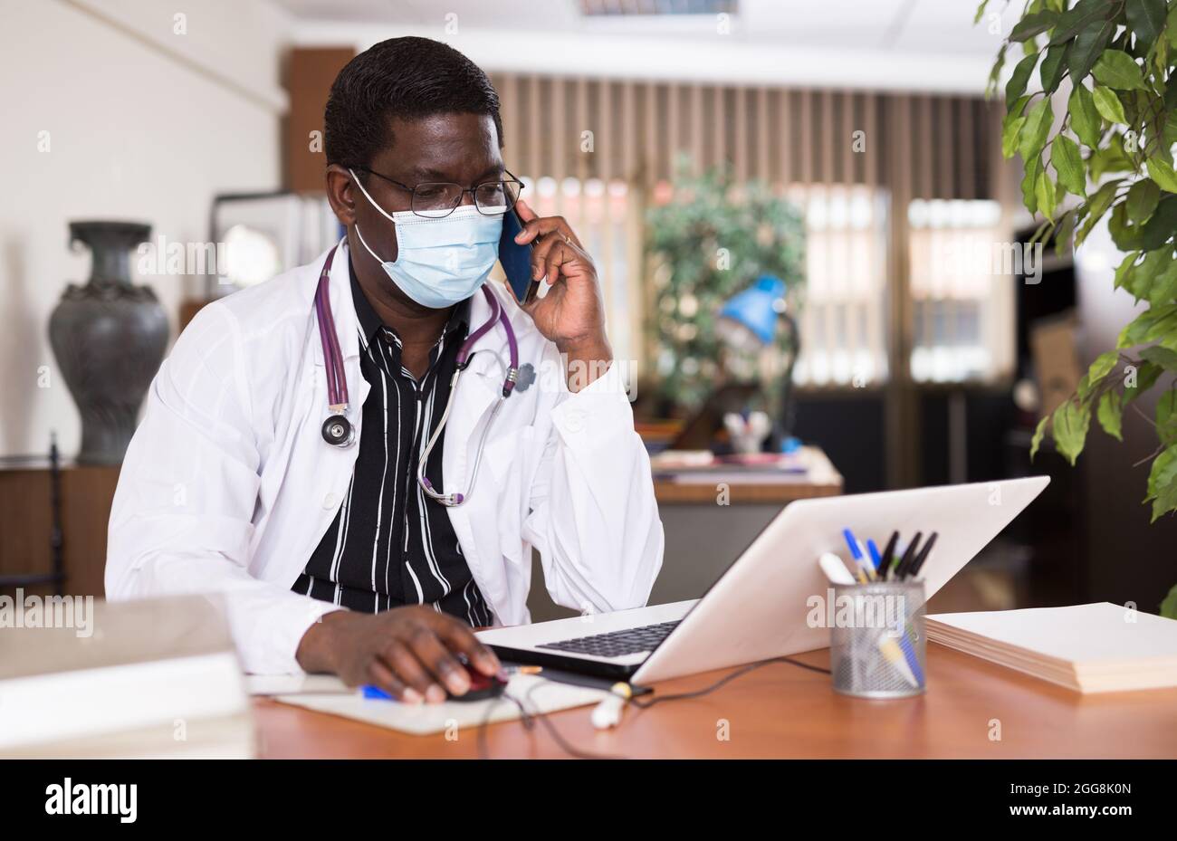 Doctor in protective mask working in medical office using laptop Stock ...