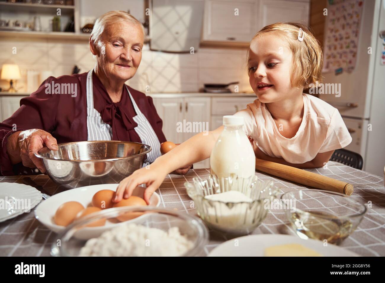 Lively girl reaching for egg in plate for cooking Stock Photo - Alamy