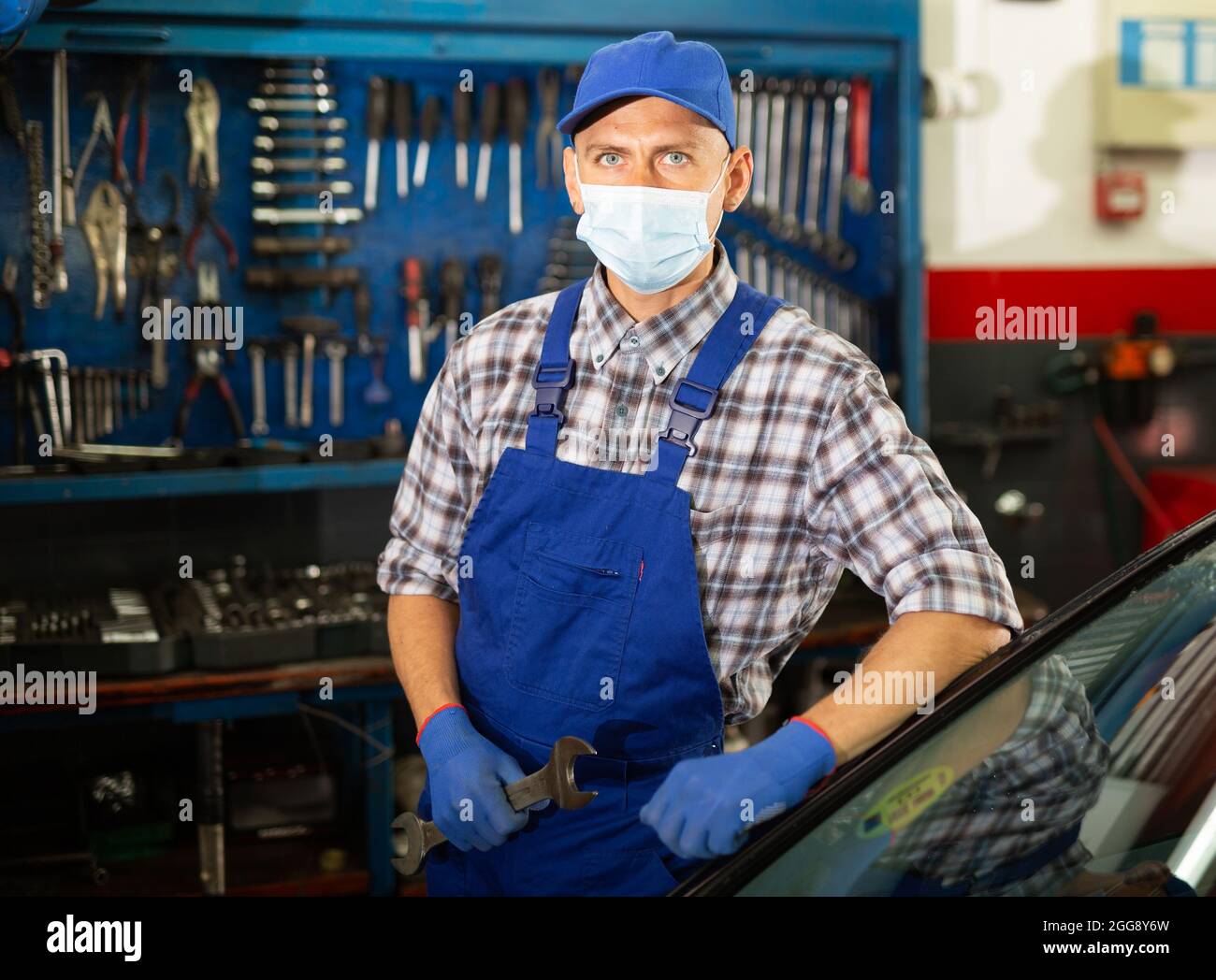 Workman in protective mask standing near car at auto repair service ...