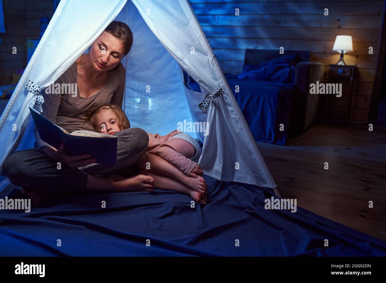 Mother with storybook helping her daughter to fall asleep Stock Photo ...