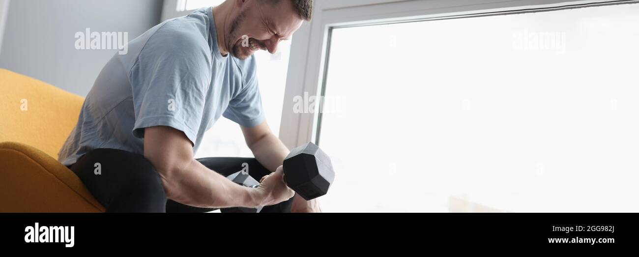Young man sitting on chair and lifting heavy dumbbell Stock Photo - Alamy