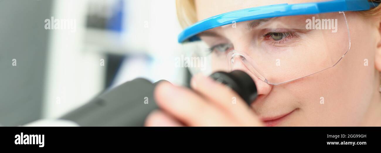 Woman chemist in safety glasses looking through microscope Stock Photo ...