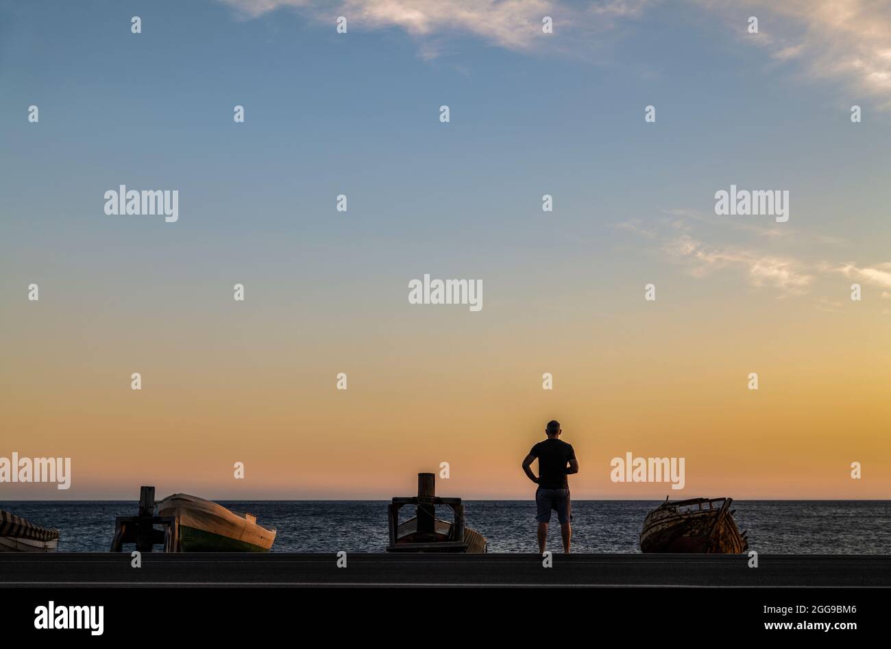 Silhouette of adult man looking at view on beach with fishing boat and ...
