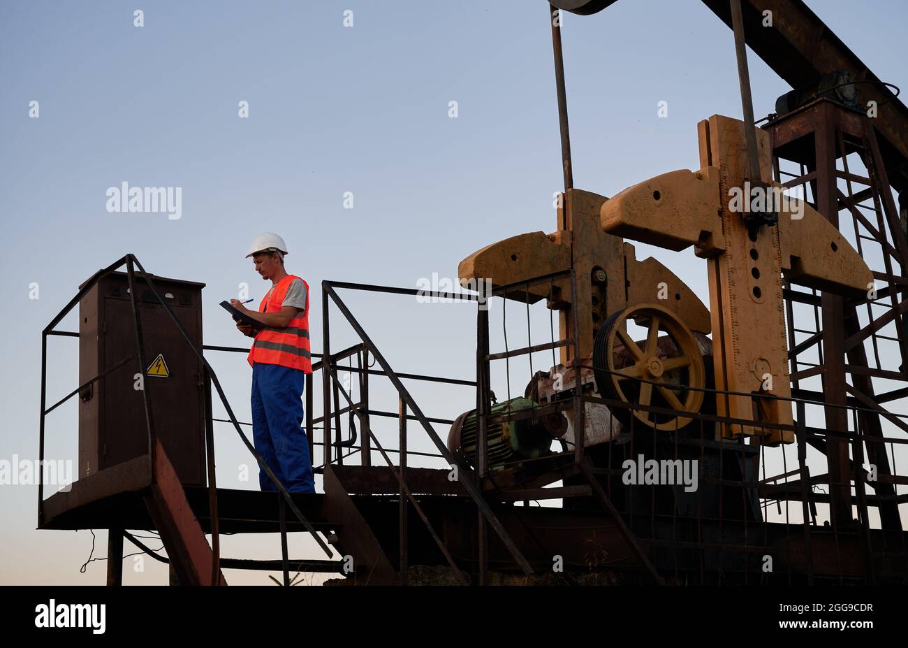 Oilman in work overalls, standing on oil rig and recording performance ...