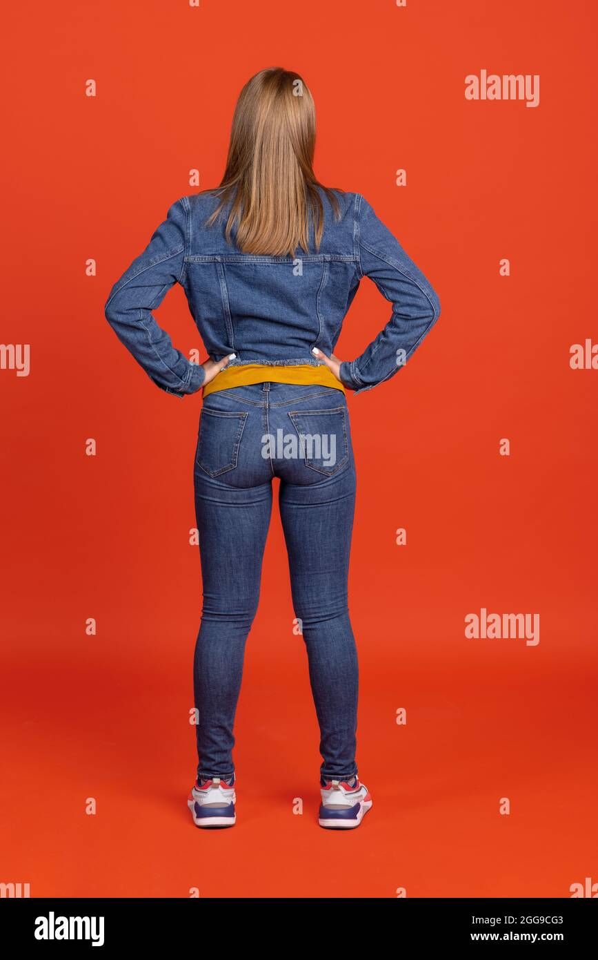 Back view of young red-headed woman standing isolated over red studio ...