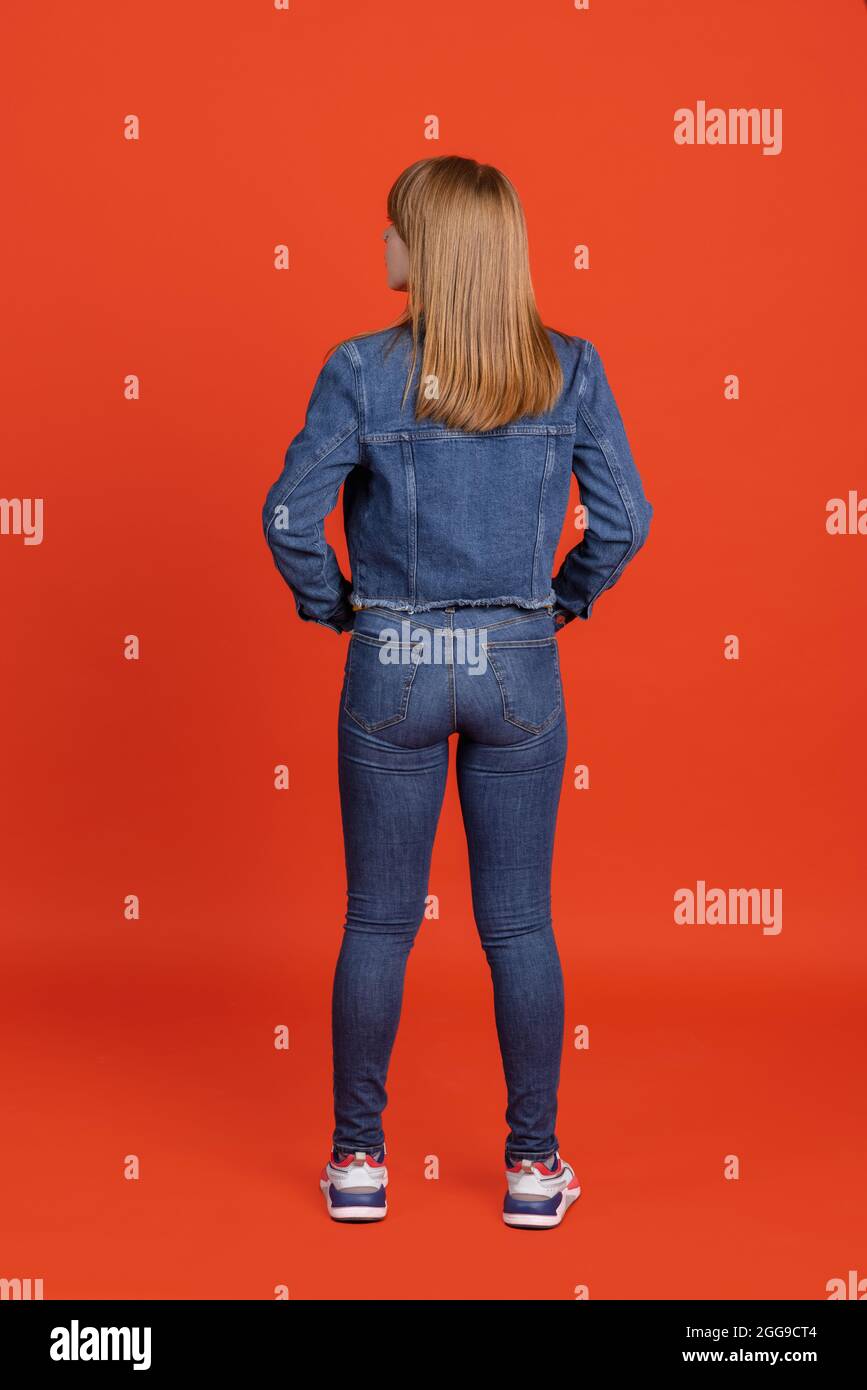 Back view of young red-headed woman standing isolated over red studio ...