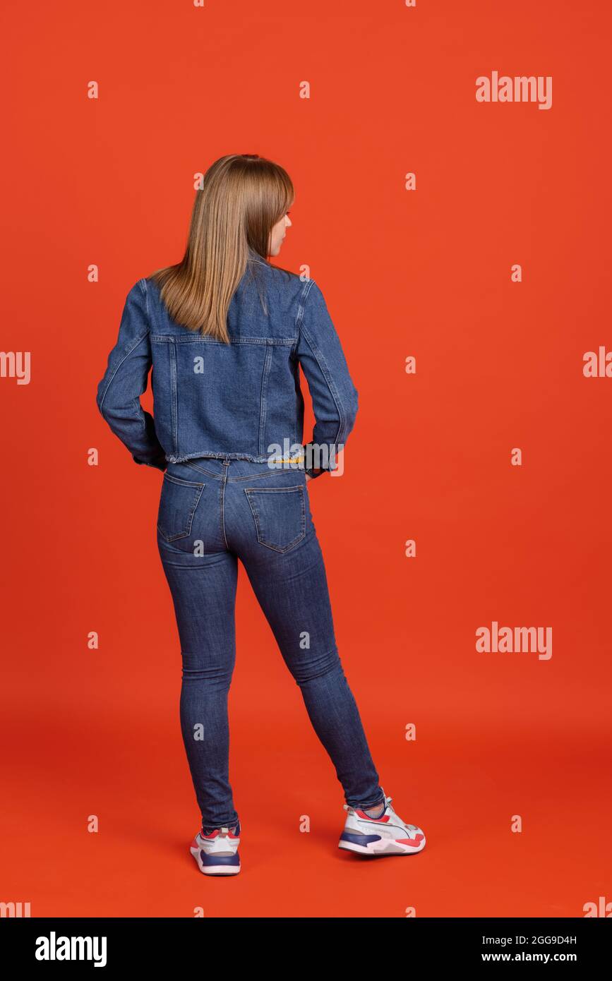 Back view of young red-headed woman standing isolated over red studio ...