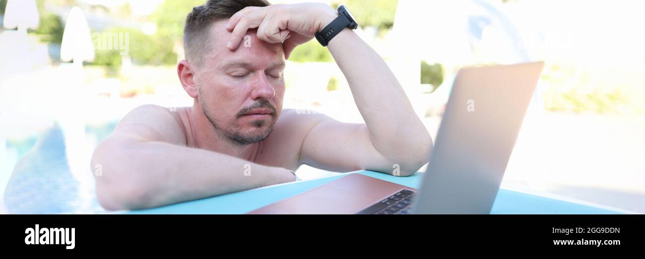 Tired young man with closed eyes in front of laptop stands in pool ...