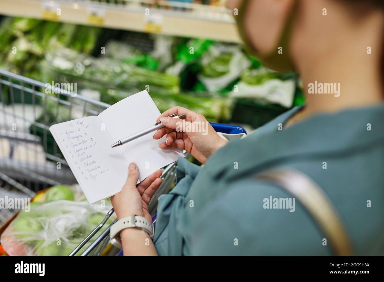 Over shoulder view of woman marking positions of shopping list with pen ...