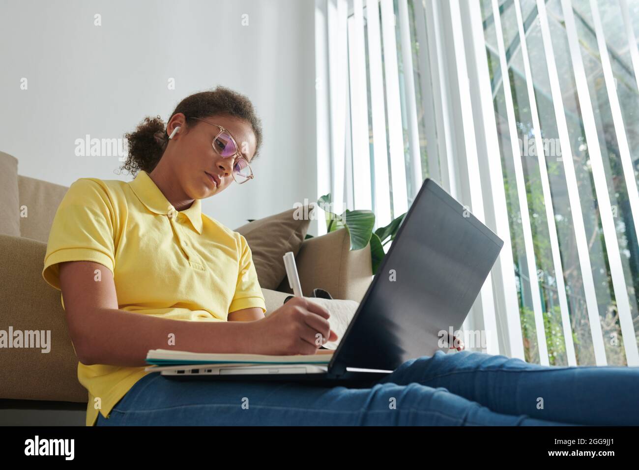 Serious schoolgirl attending online math class and writing down ...
