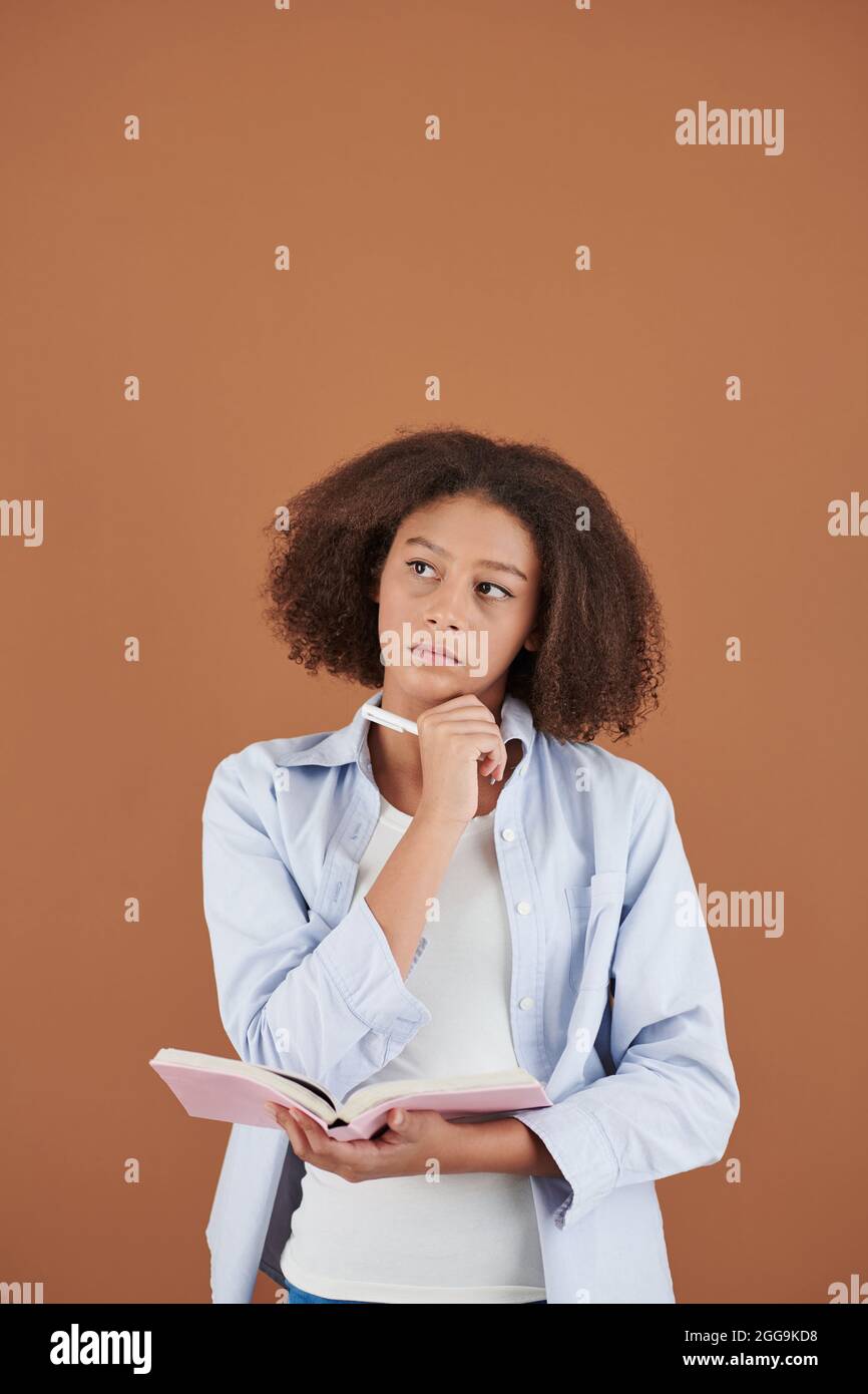 Studio portrait of pensive teenage girl taking notes in her diary or ...