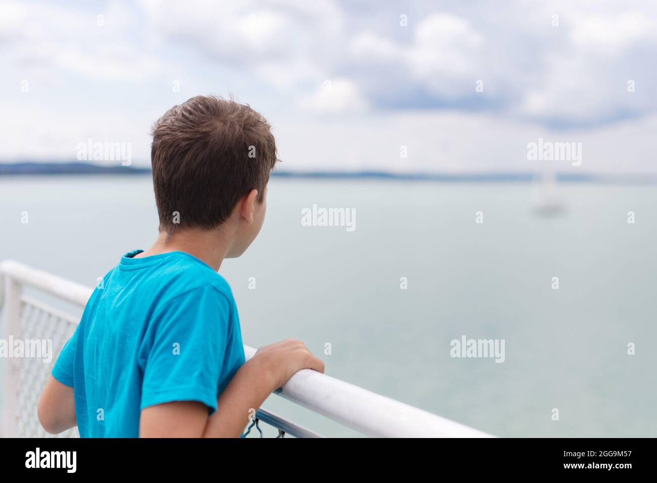 Little boy watching sailboat in the distance on sea, cruise ship ...