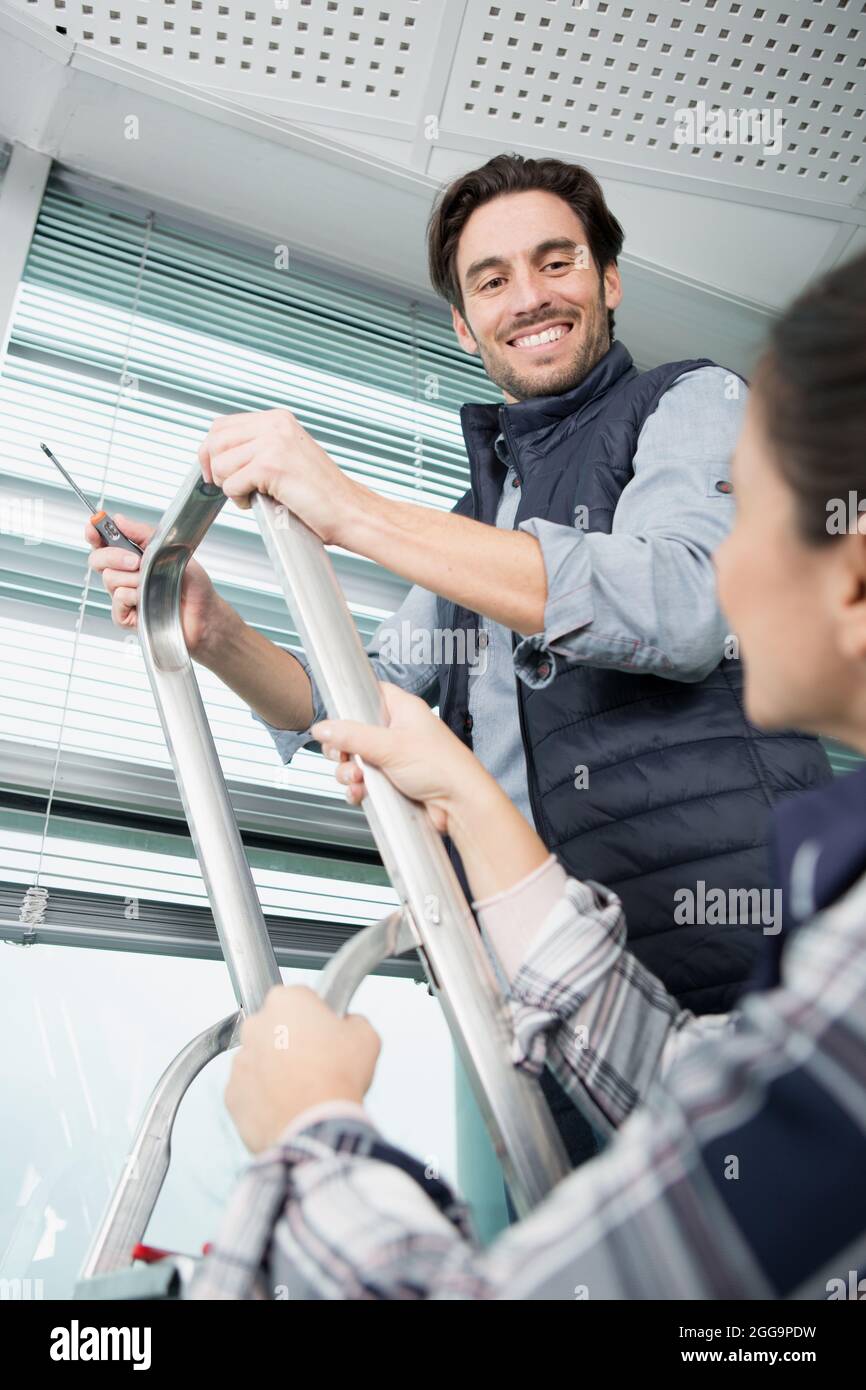 woman securing stepladder while man fixes window blind Stock Photo - Alamy