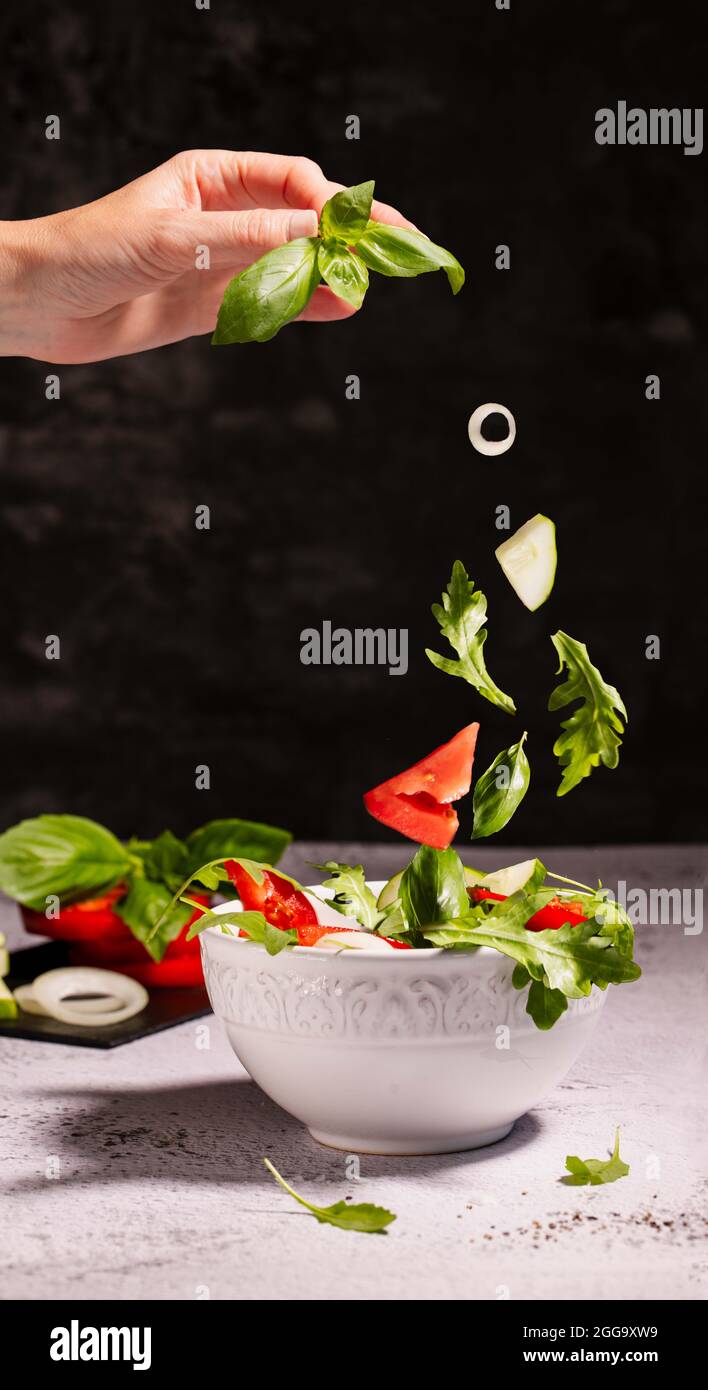 A hand placing bazil leaves into a while bowl with falling salad ...
