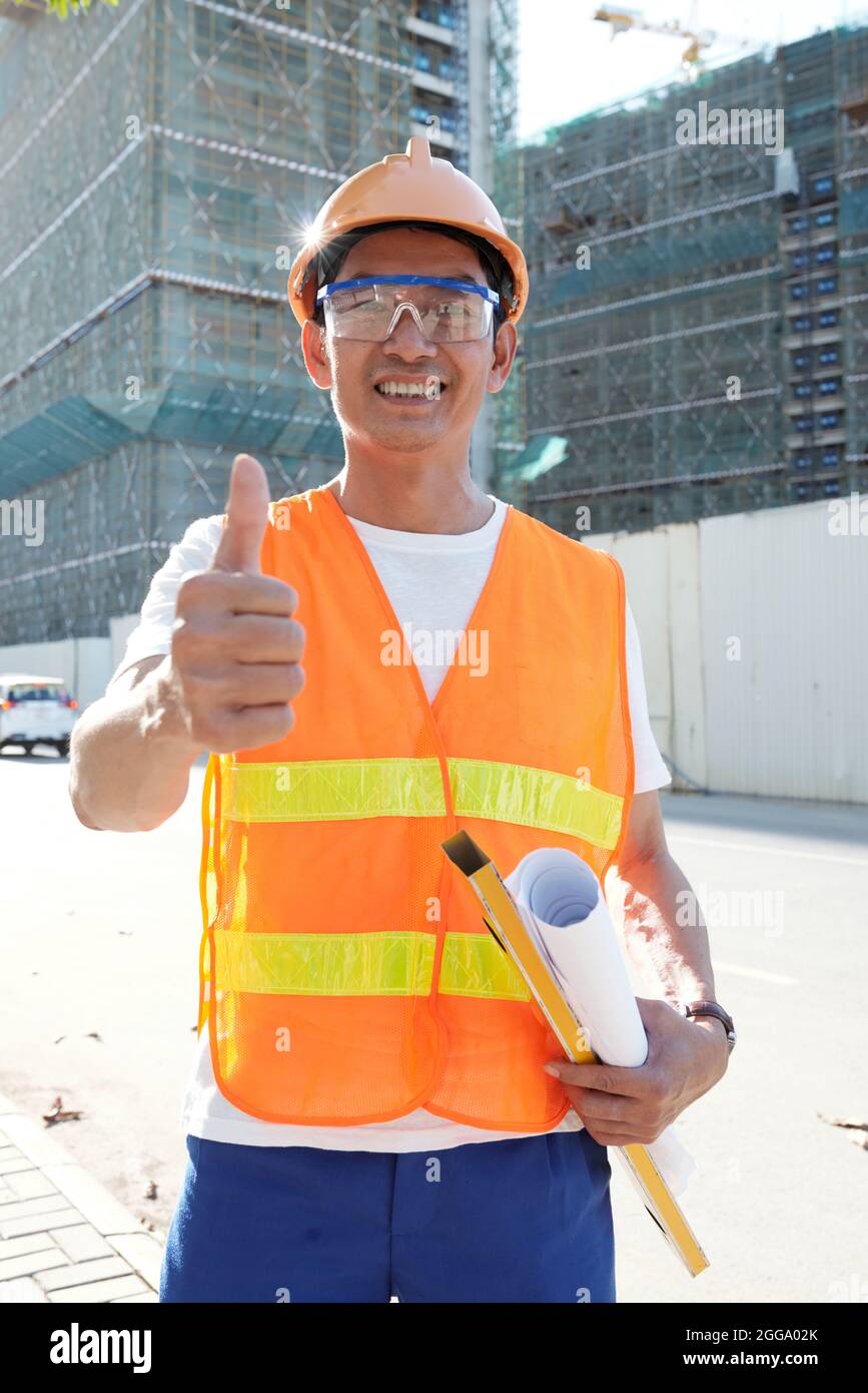 Happy head engineer standing at construction site with level and rolled ...
