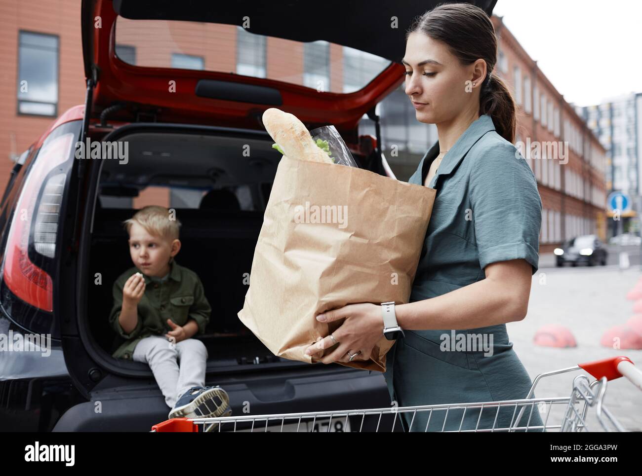 Content young mother in watch putting full paper bag in car trunk while ...