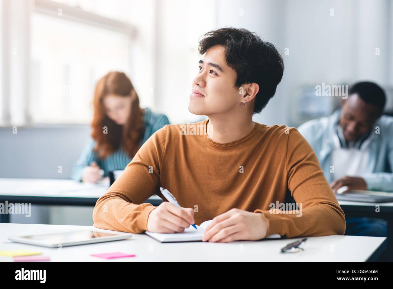 Smiling asian student sitting at desk in classroom thinking Stock Photo ...
