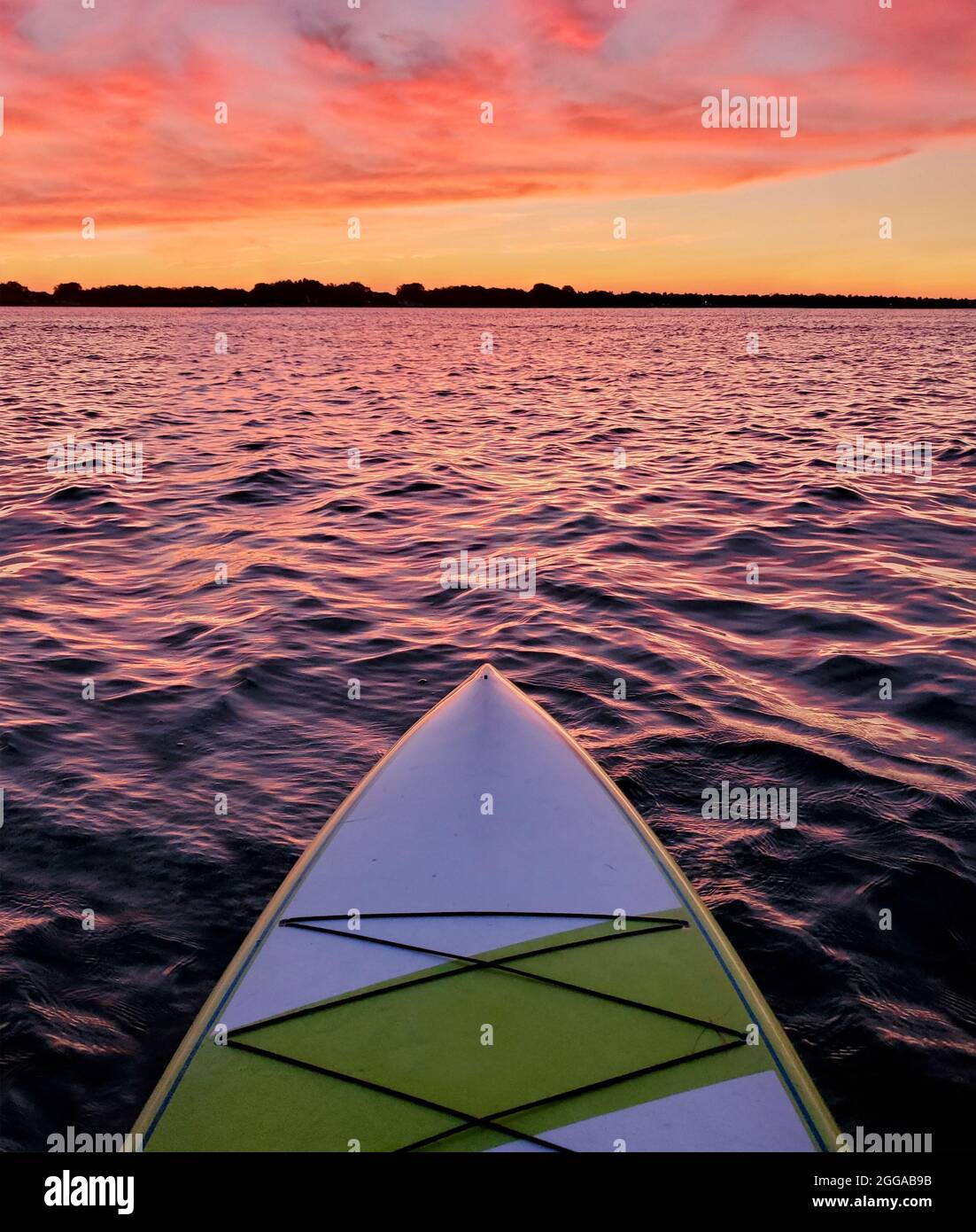 A Paddleboard floating on calm water at dusk with the colorful light of ...