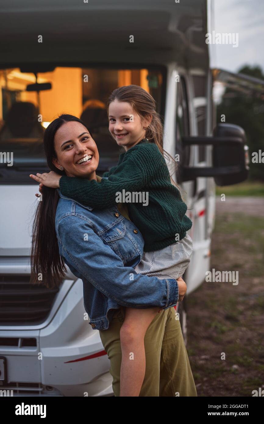 Mother with daughter standing by car outdoors in campsite at dusk ...