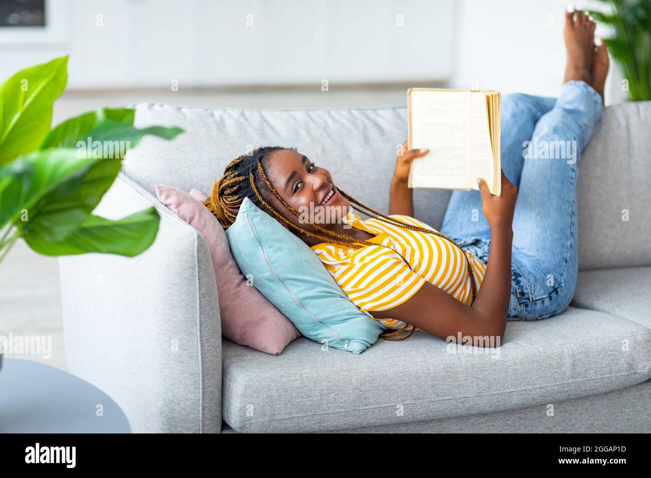 Carefree black woman reclining on couch, reading book Stock Photo - Alamy