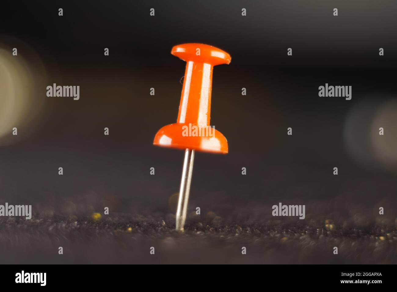 Orange push pin stuck on a black surface Stock Photo - Alamy