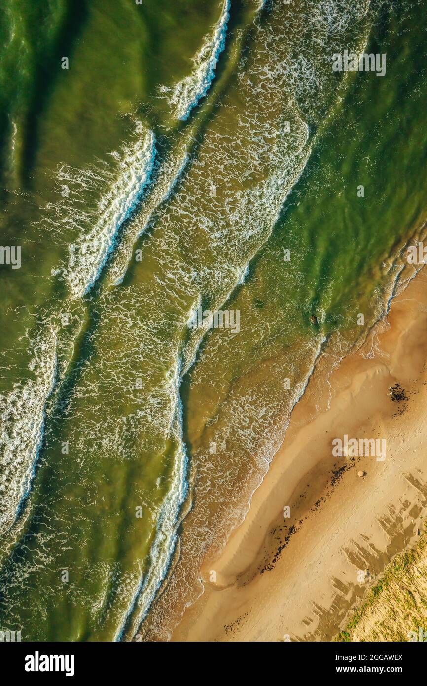 Vertical top view shot of a beach being washed off by the waves of a ...