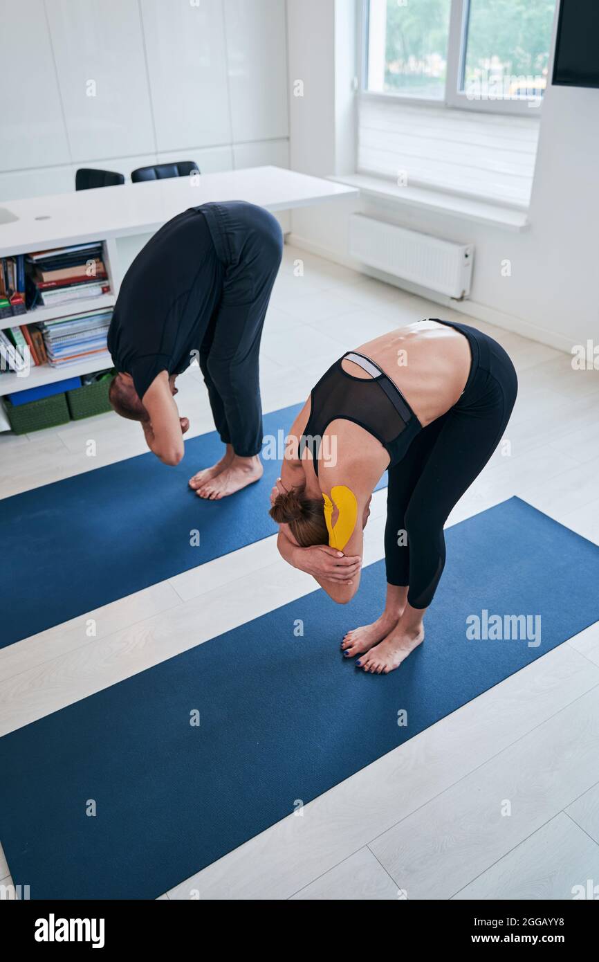 Pretty woman and man in black clothes practicing forward fold yoga pose ...