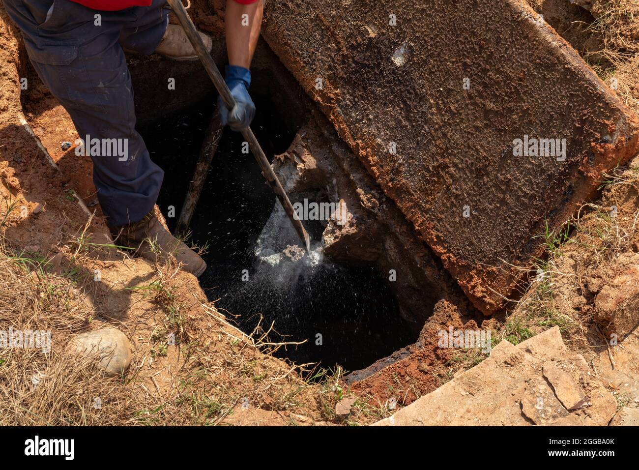 Man breaking apart a wastewater outlet in an old septic tank to bring ...