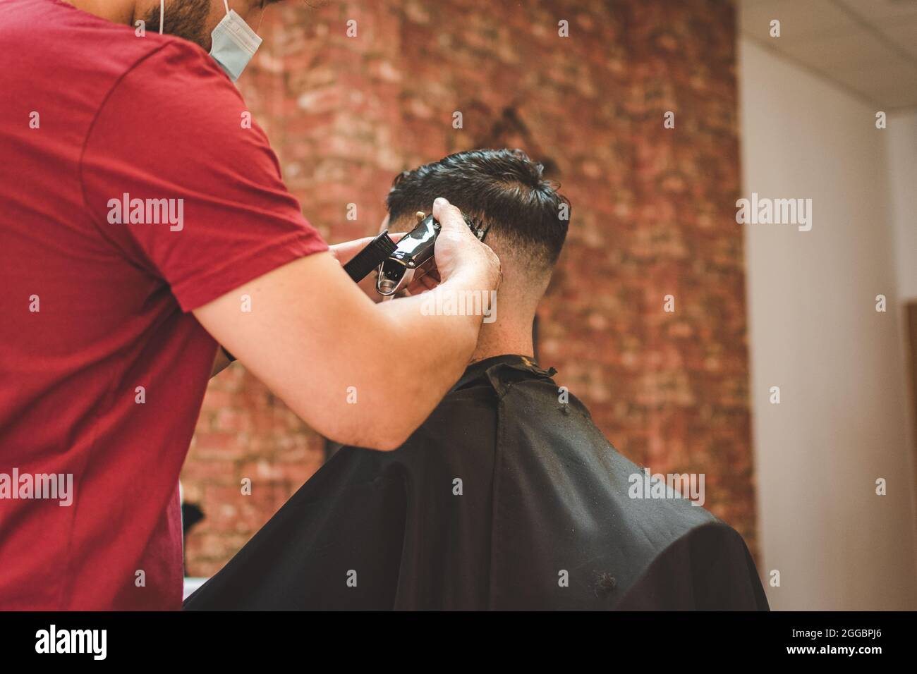 hairdresser giving a client wearing a mask a haircut with a clippers ...