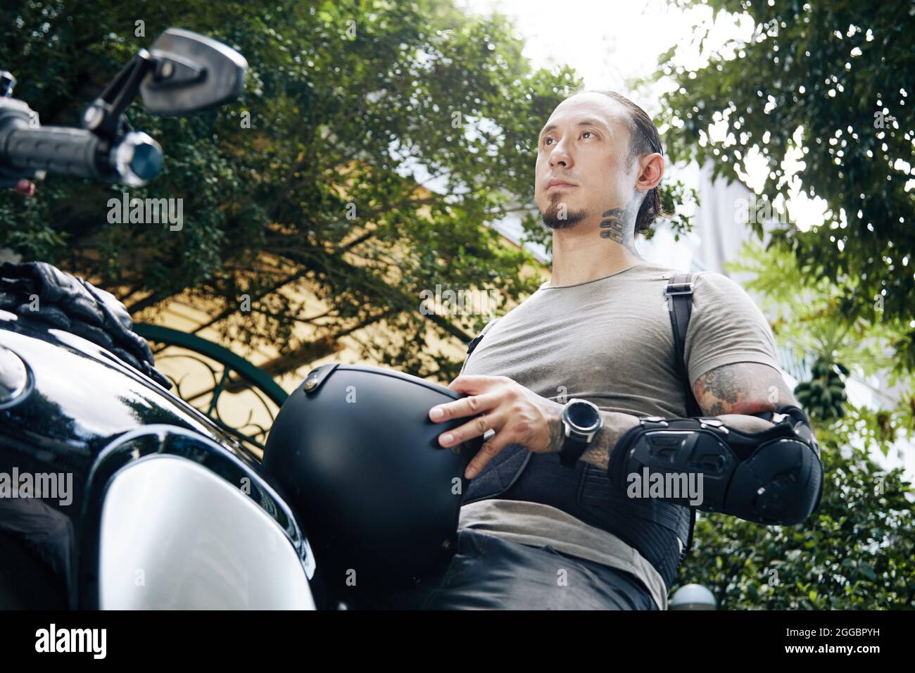 Serious young man with helmet sitting on motorcycle and taking off ...
