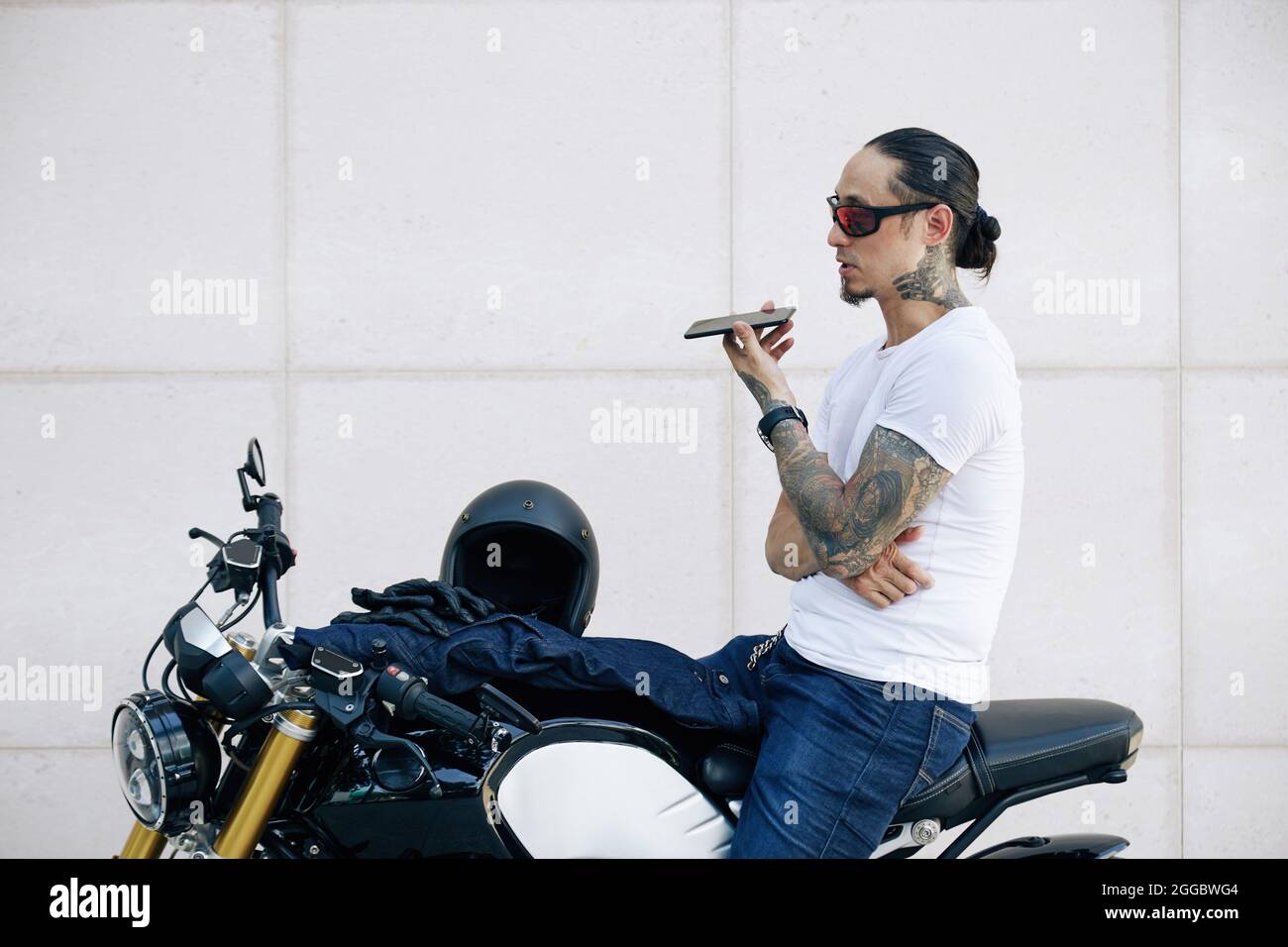 Fit muscular man in glasses sitting on motorcycle and recoding voice ...