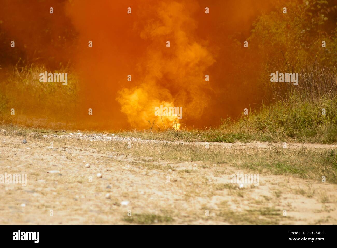 Smoke signal bomb. An orange smoke bomb is lit next to a dirt road ...