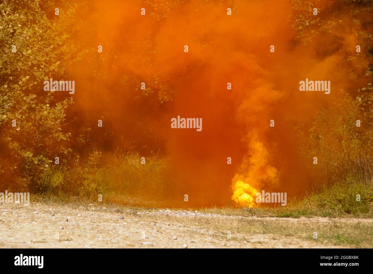 Smoke signal bomb. An orange smoke bomb is lit next to a dirt road ...