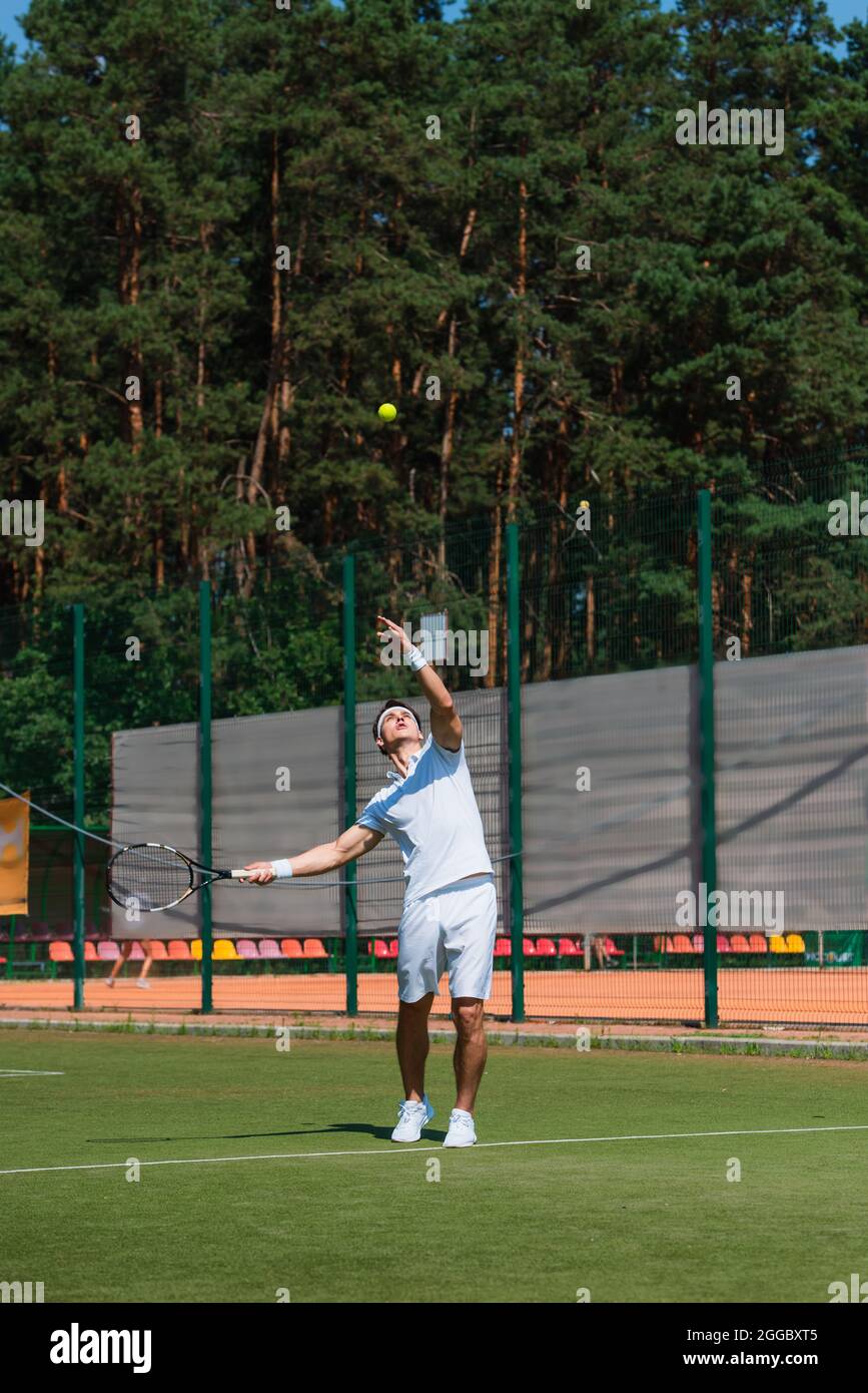 Young sportsman with racket throwing ball while playing tennis on court ...