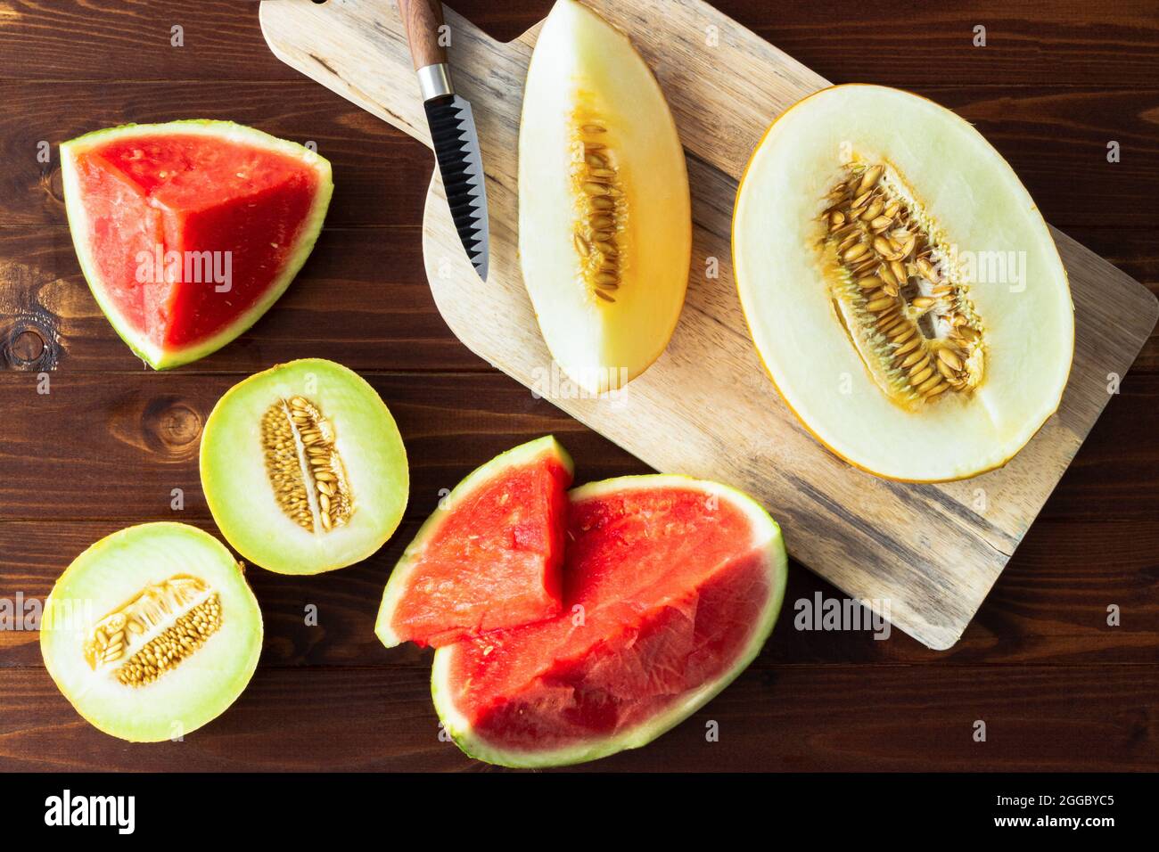 Top view of variety of melons on wooden cutting board and rustic wood ...