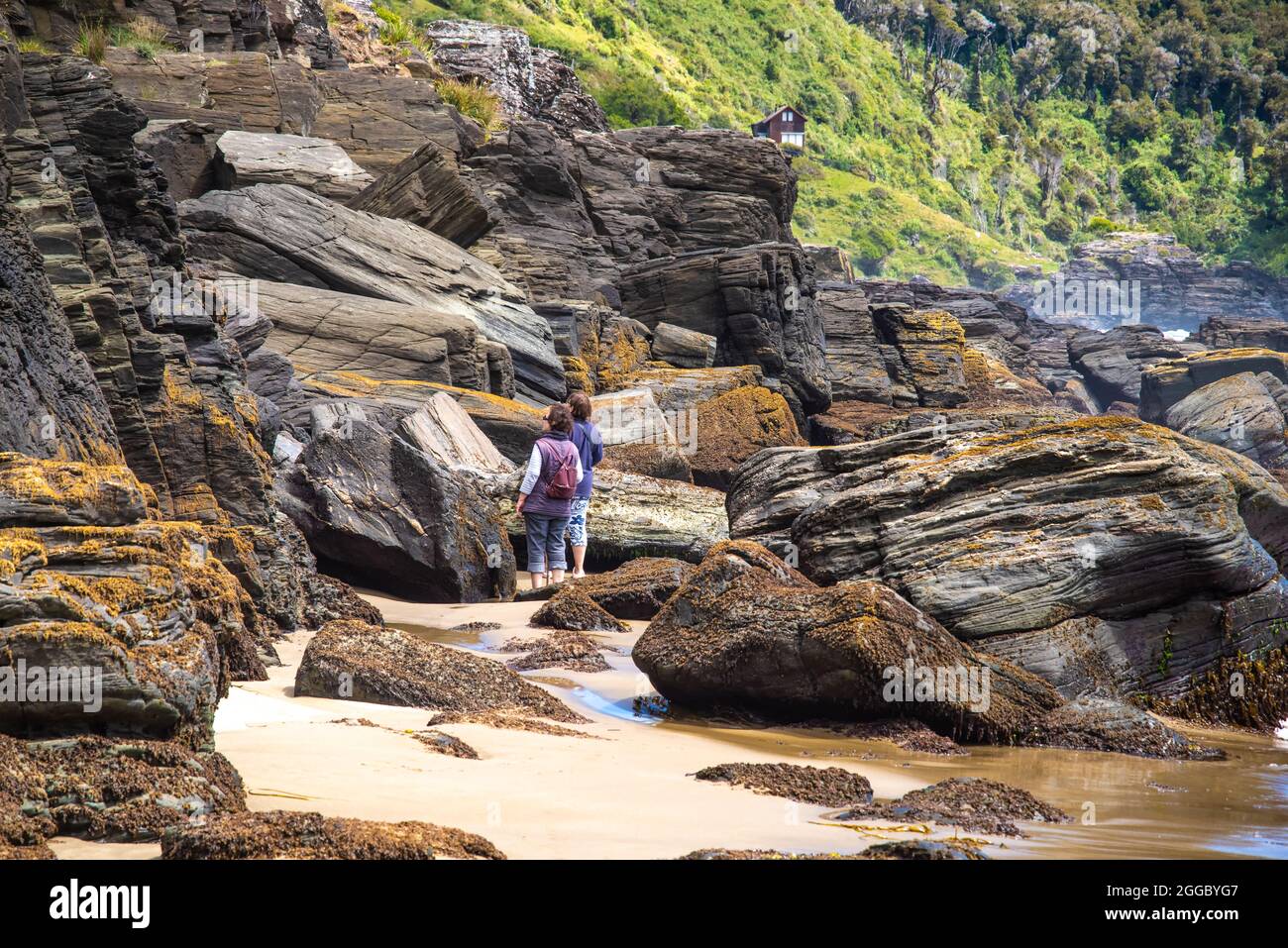 Female travelers exploring a rocky coast of the Pacific in Los Lagos ...