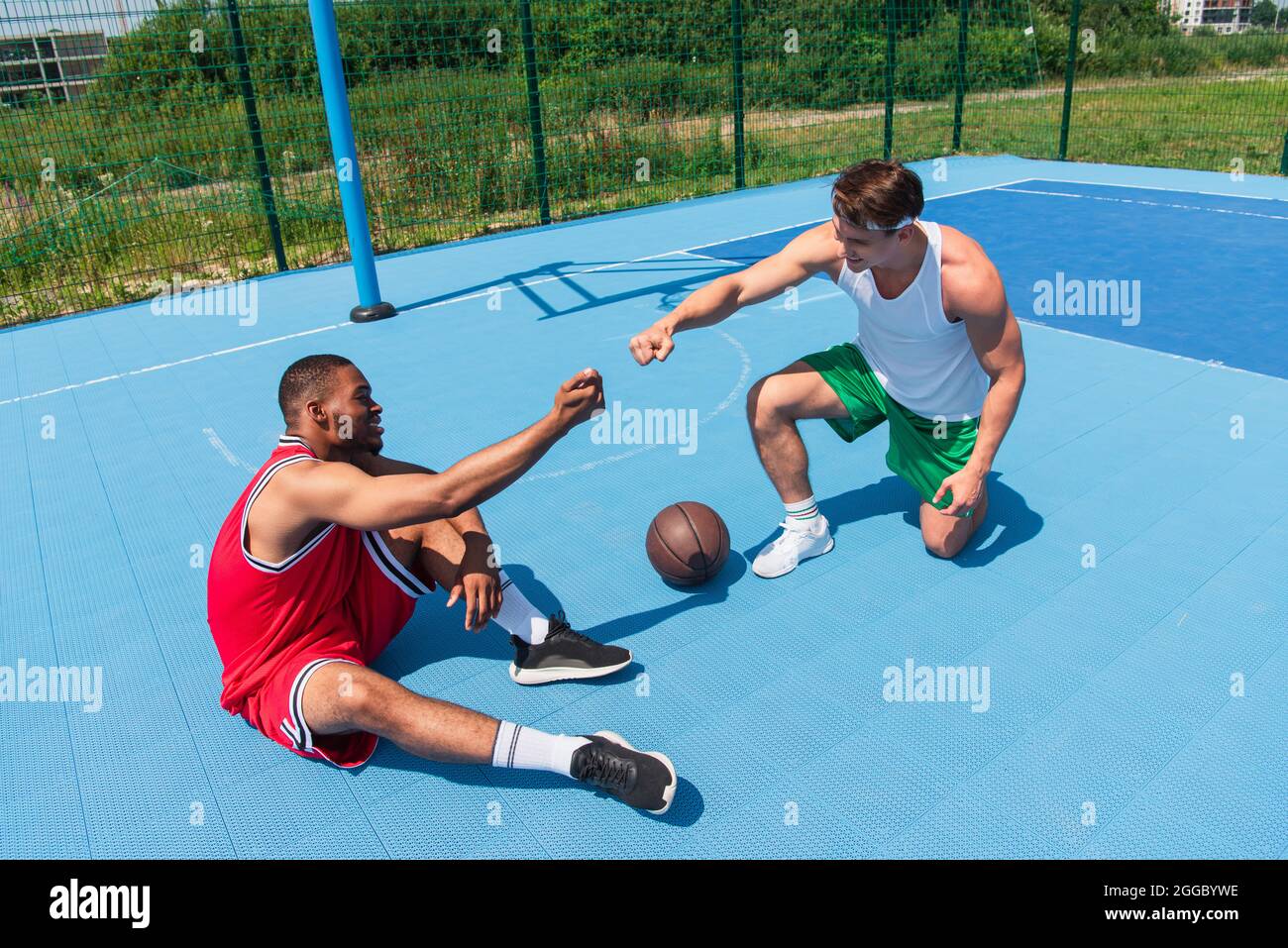 Smiling multiethnic basketball players doing fist bump on playground ...
