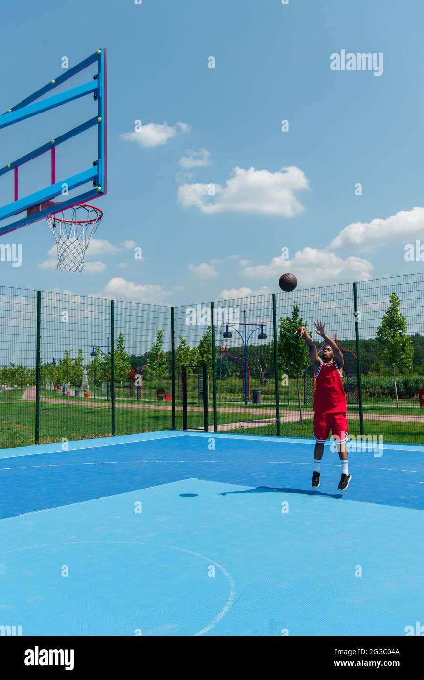 African american sportsman jumping and throwing basketball ball in hoop ...