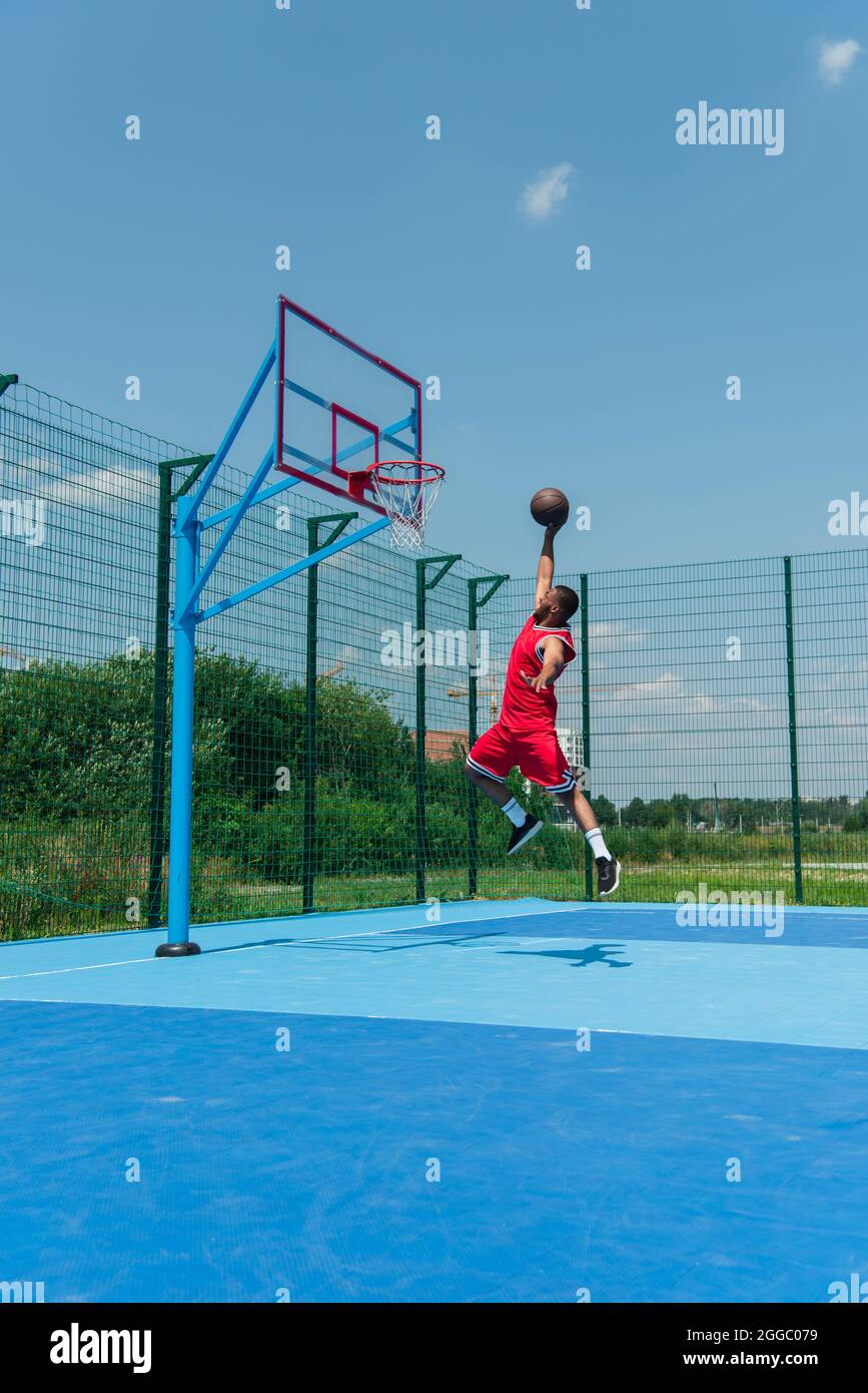 Side view of african american sportsman jumping under hoop while ...