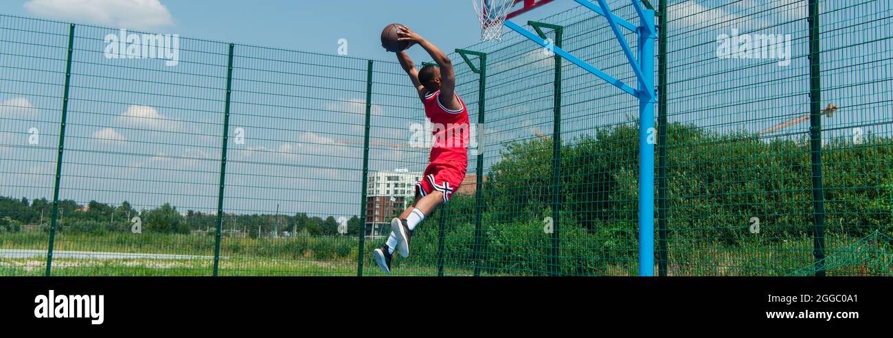 African american sportsman with basketball ball jumping near hoop ...